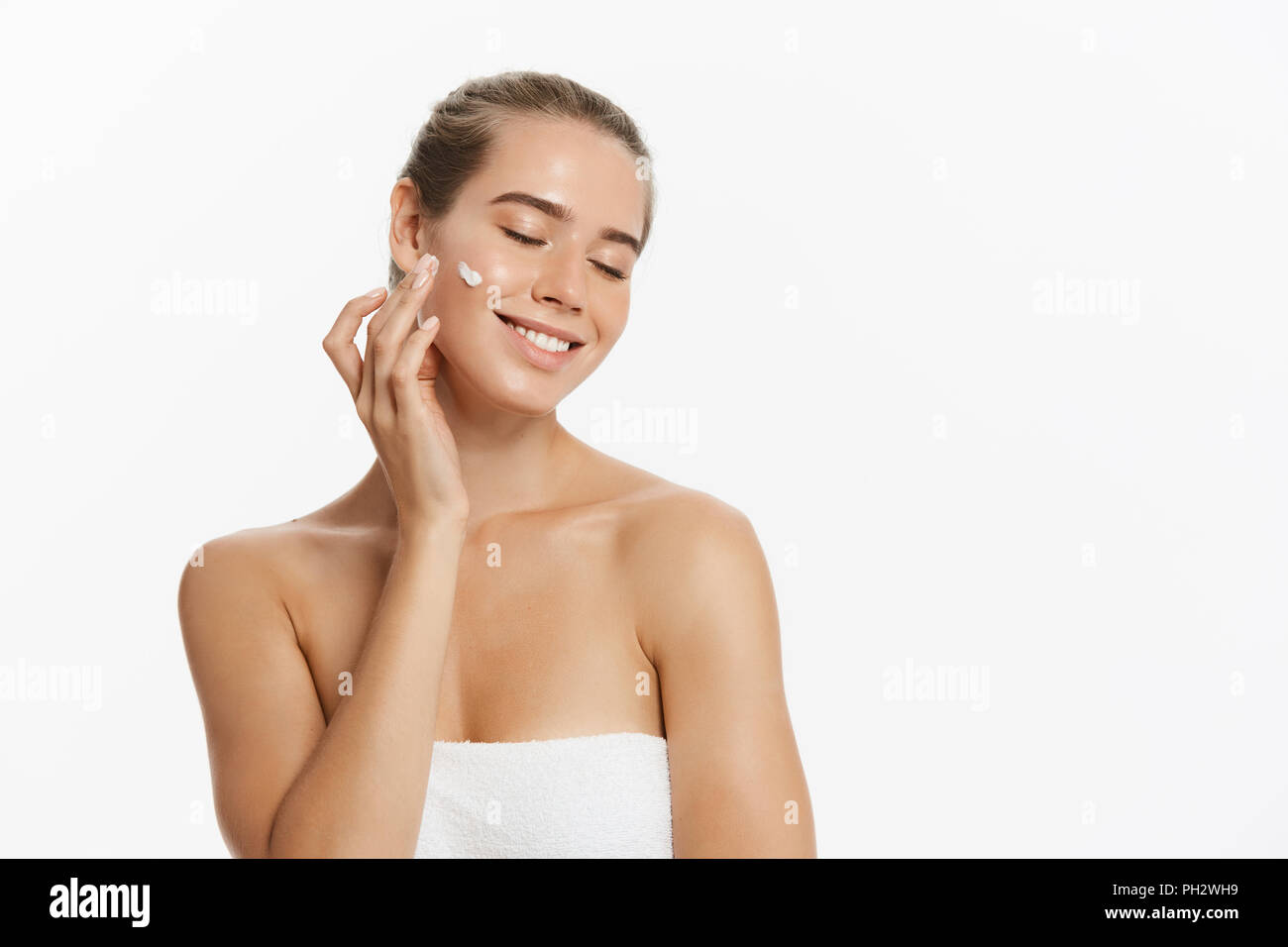 Beautiful young woman applying cosmetic cream treatment on her face isolated on white background ...