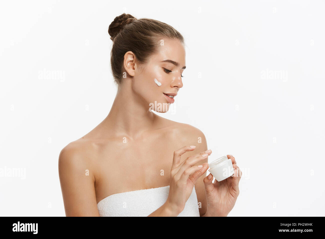 Beautiful young woman applying cosmetic cream treatment on her face isolated on white background ...