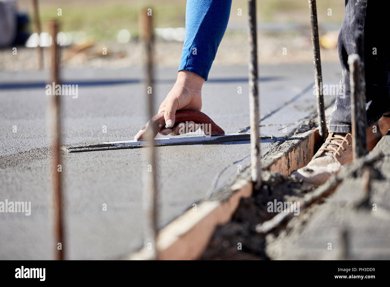 A mason using a concrete trowel to finish a newly poured concrete slab ...