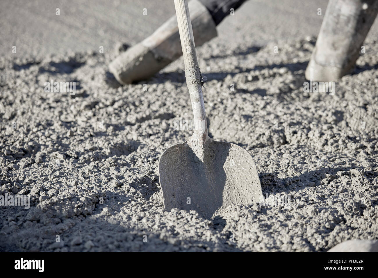 A shovel in wet cement with the boots of a mason behind it and shallow ...