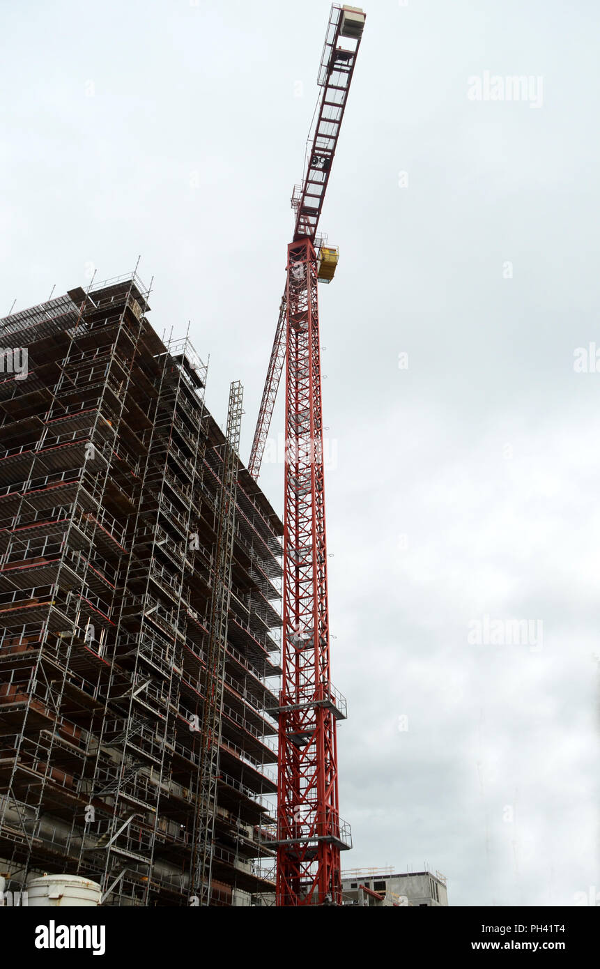 Large red construction crane besides a new building covered with ...