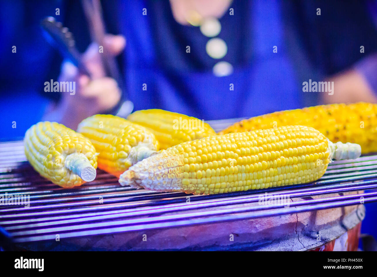 Close up hand of street food vendor while grilling for mixed sweet corn ...