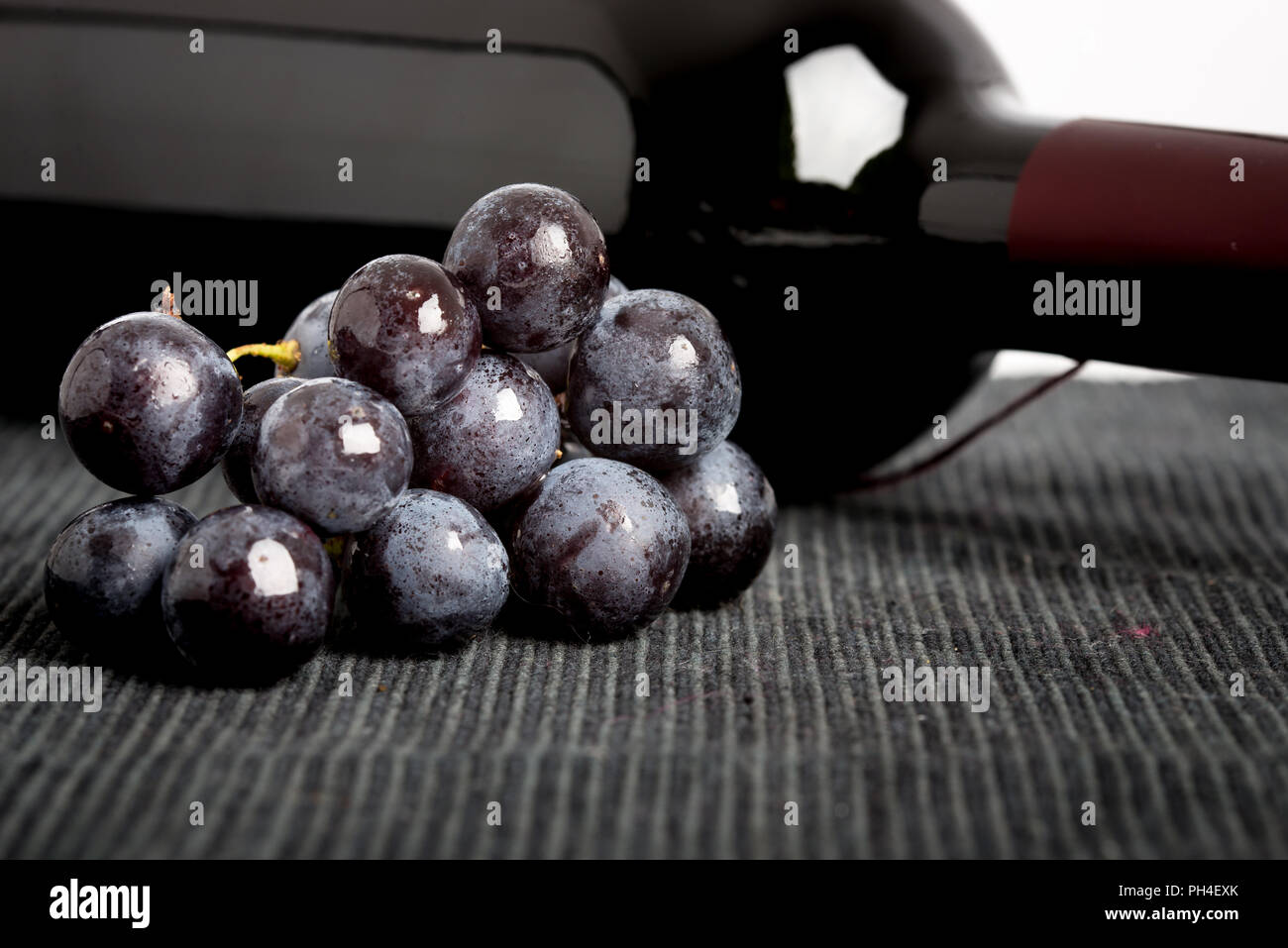 Bunch of fresh black grapes and an unlabeled bottle of red wine lying ...