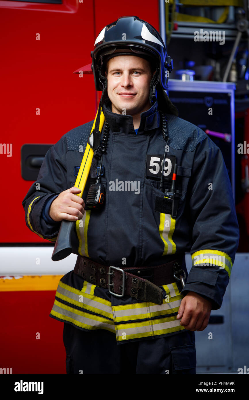 Photo of fireman wearing helmet with hammer against fire engine Stock ...