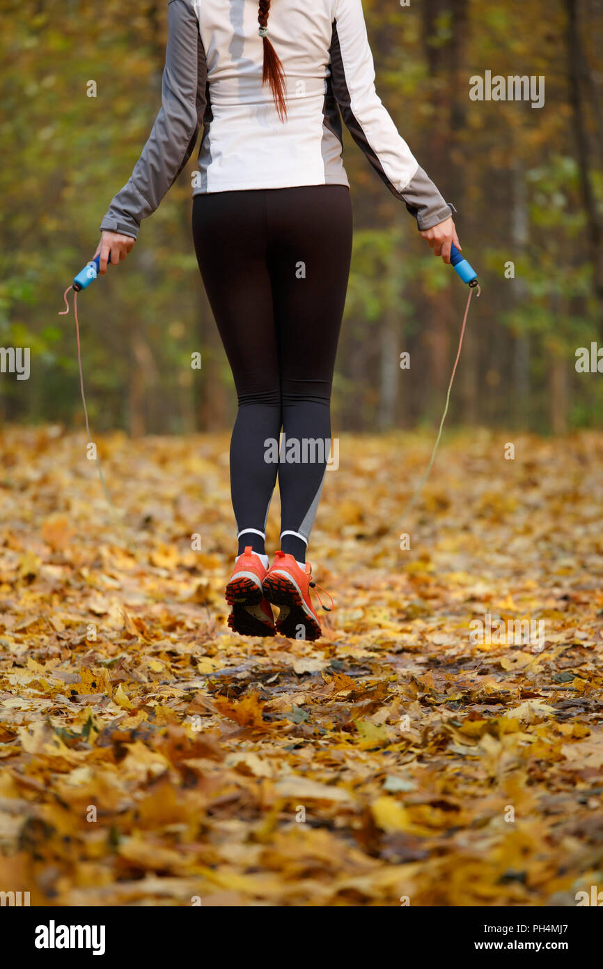 Photo from back of sports woman jumping with rope at autumn forest ...