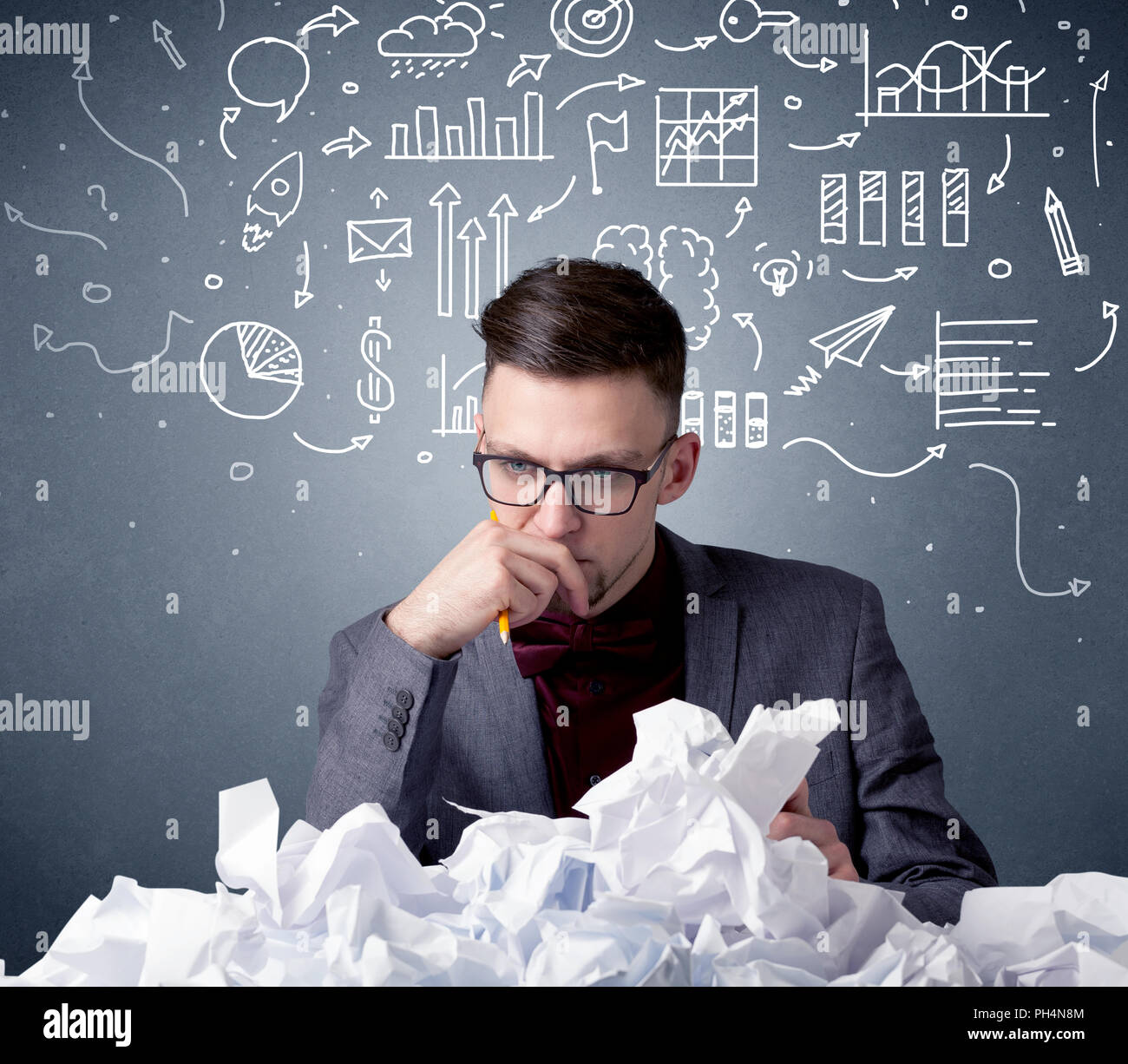 Young businessman sitting behind crumpled paper with mixed drawings ...