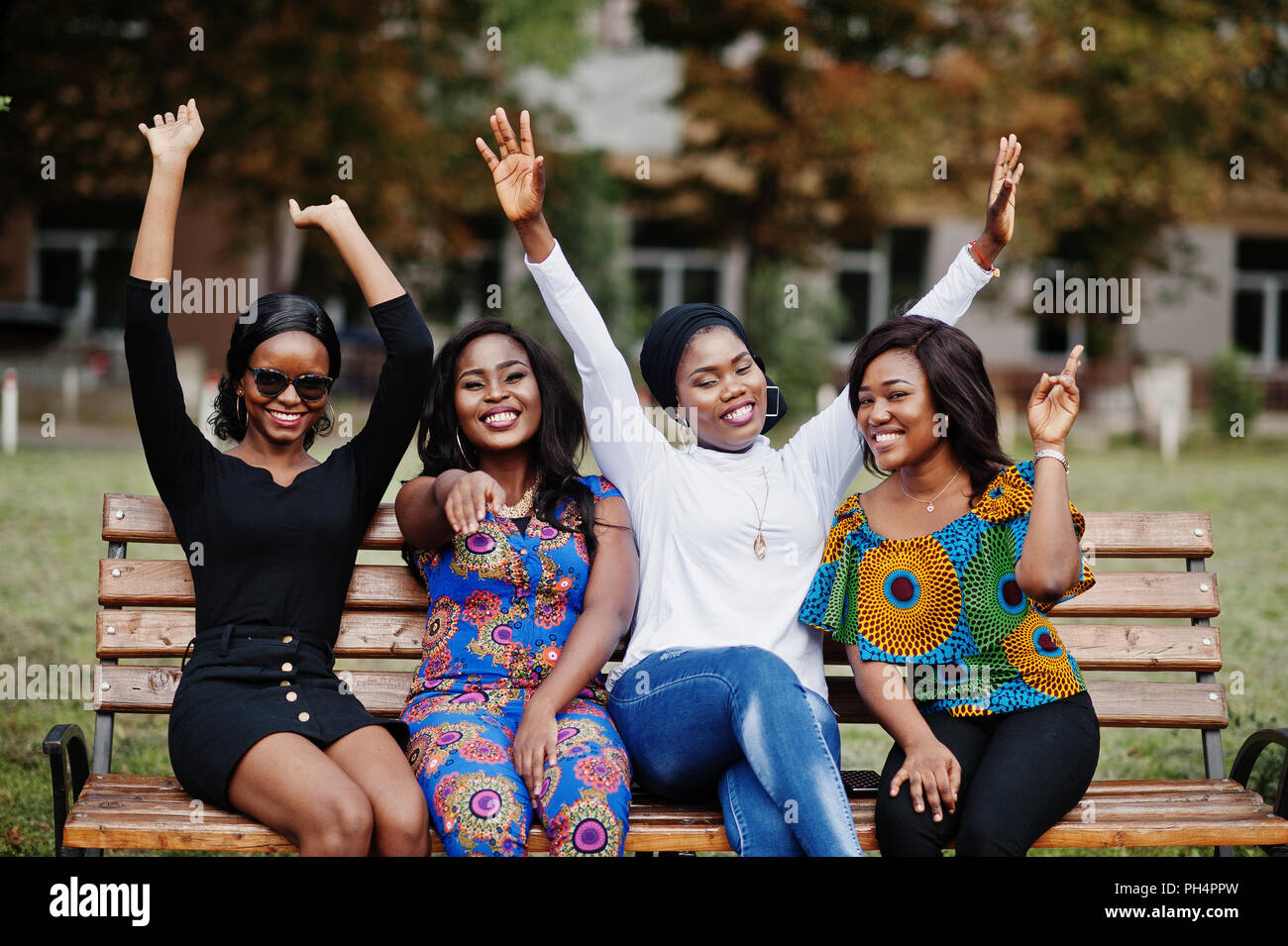 Group of four african american girls sitting on bench outdoor and put ...