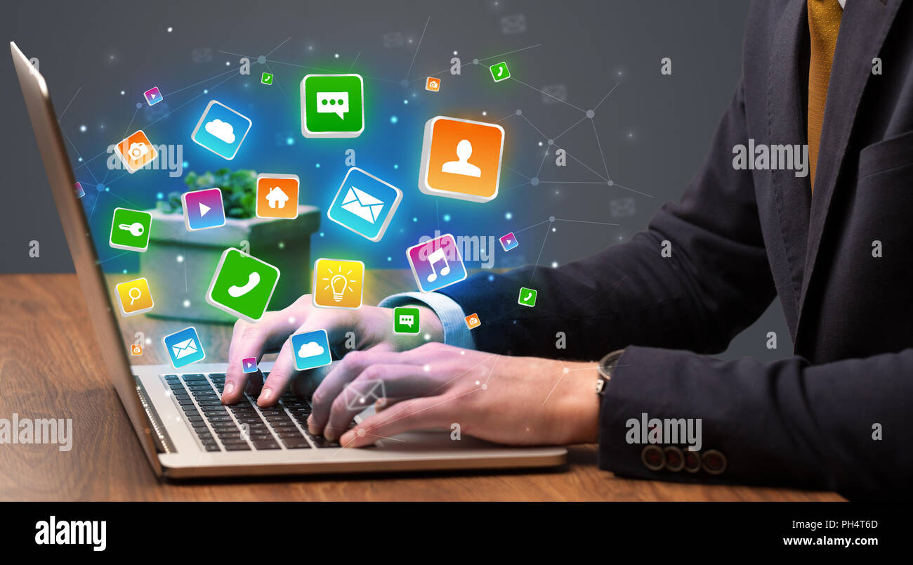 Businessman hand typing on laptop with flying application icons around ...