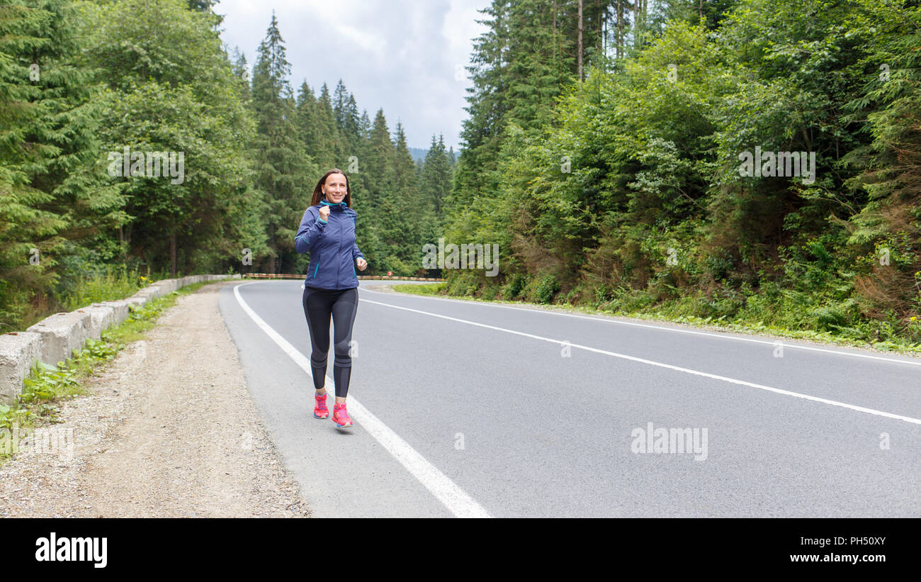 Young smiling woman jogging on mountain road. Happy girl with long hair ...
