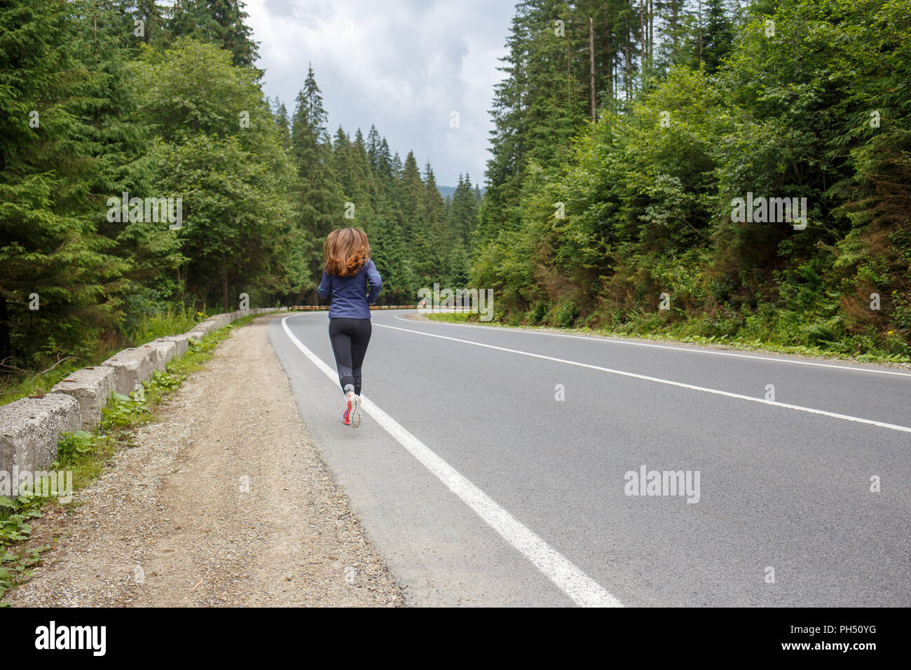 Running girl on the road. Young slim woman jogging in mountains. Rear ...