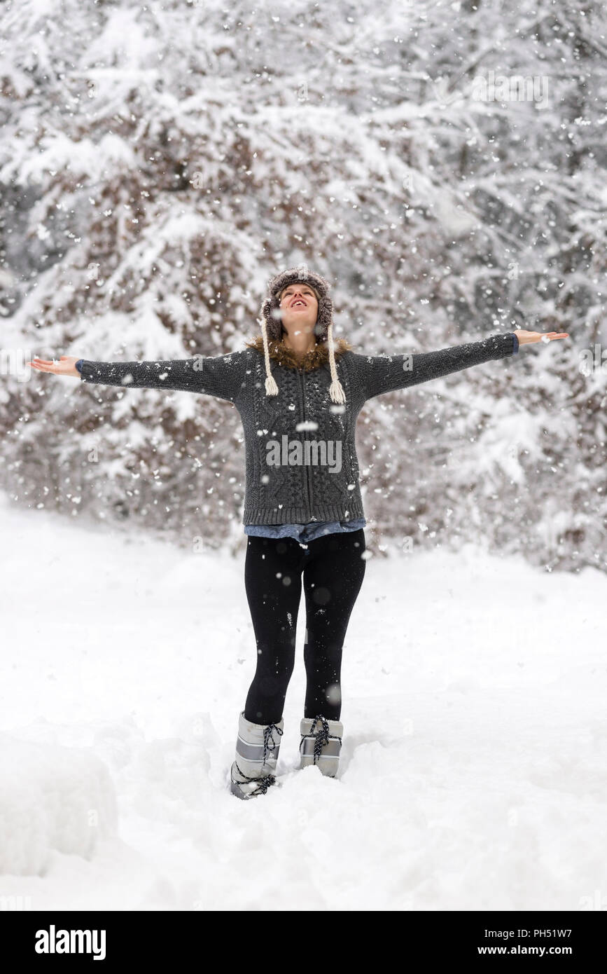 Woman standing in a snowy woodland welcoming snowflakes and celebrating ...