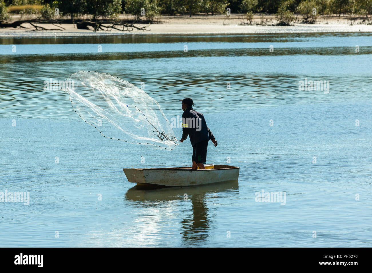 Fisherman casting net action fishing from small boat into river lagoon ...