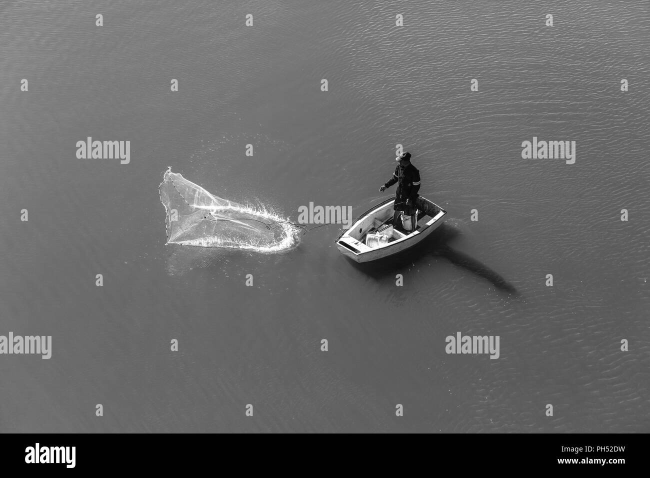Fisherman casting net action fishing from small boat into river lagoon ...