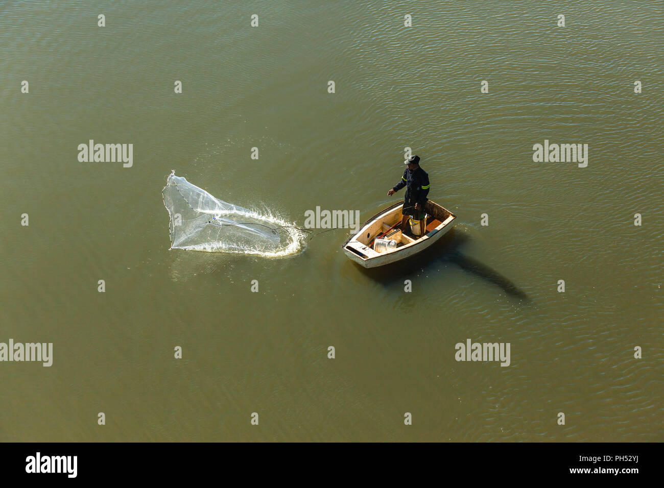 Fisherman casting net action fishing from small boat into river lagoon ...