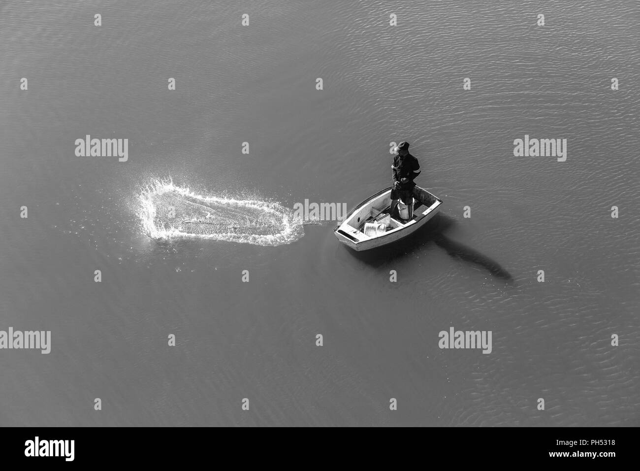 Fisherman casting net action fishing from small boat into river lagoon ...