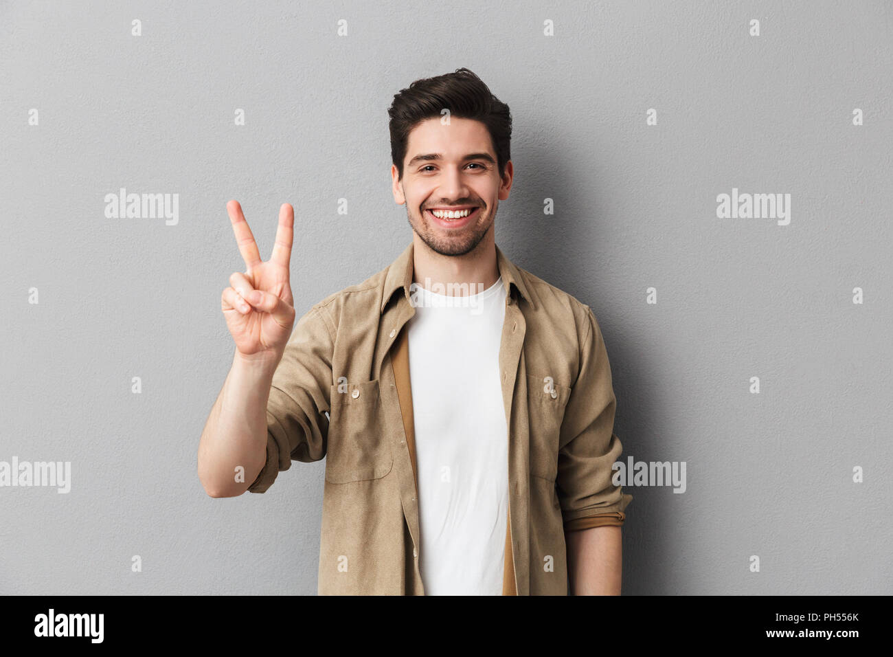 Portrait of a happy young casual man showing peace gesture isolated ...