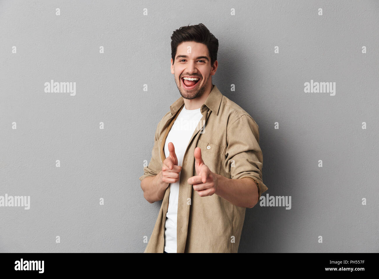 Portrait of a cheerful young casual man pointing at camera isolated ...