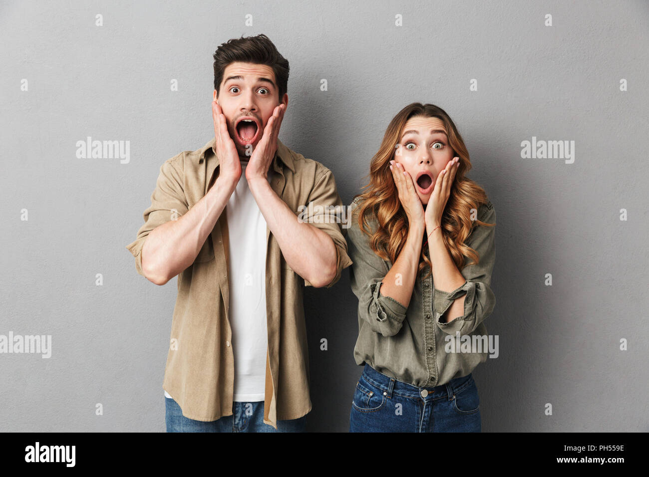 Portrait of a shocked young couple standing together isolated over gray ...