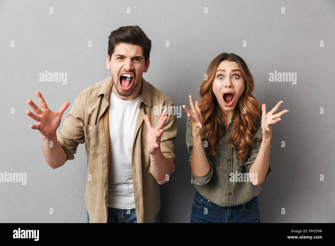 Portrait of a shocked young couple standing together isolated over gray ...