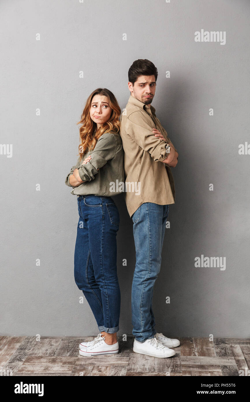 Full length portrait of a sad young couple standing back to back with ...