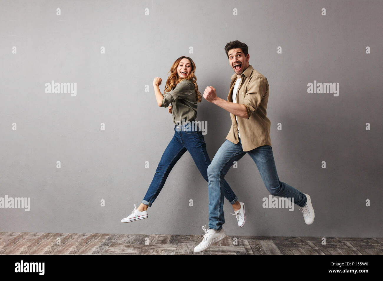 Full length portrait of a happy young couple jumping together and ...