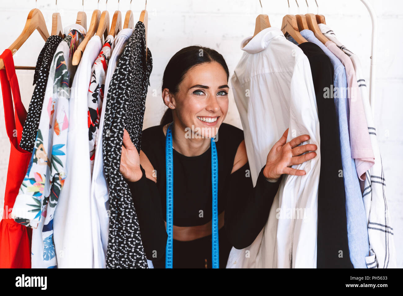 Cheerful young woman clothes designer standing at the clothes rack ...