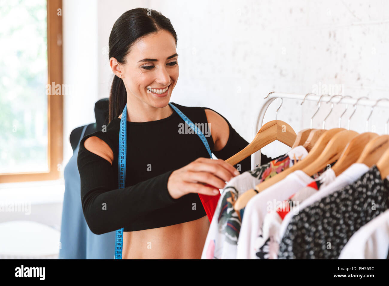 Attractive young woman clothes designer standing at the clothes rack ...
