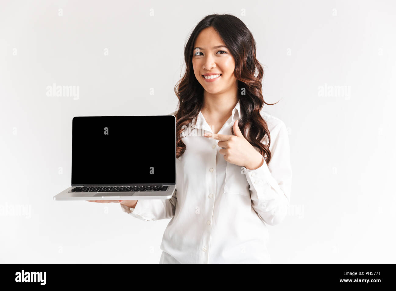 Smiling young asian businesswoman pointing at black screen laptop computer over white background ...