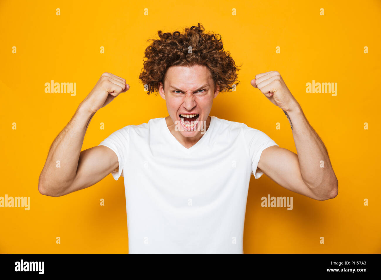 Photo of strong curly man 20s in casual t-shirt screaming and showing ...