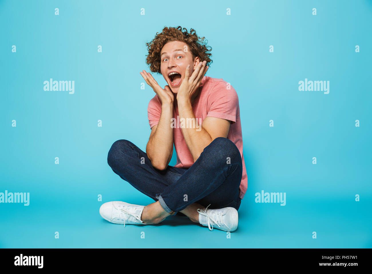 Portrait of a cheerful young curly haired man screaming sitting with ...