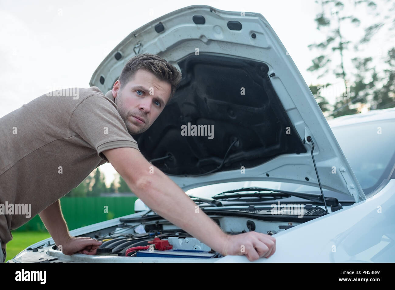 young stressed man having trouble with his broken car looking in ...