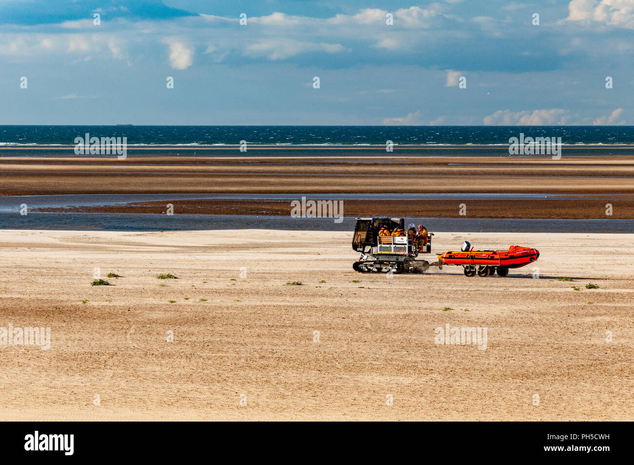 An RNLI rigid inflatable boat and crew in a tractor going across ...