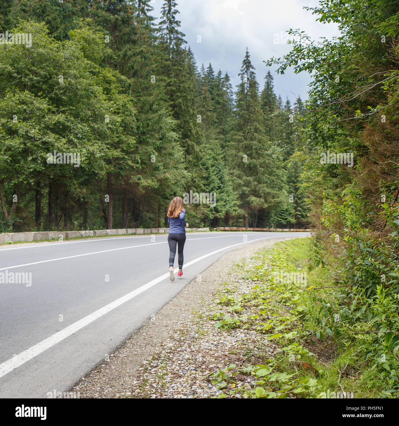 Running girl on the road. Young slim woman jogging in mountains. Rear ...
