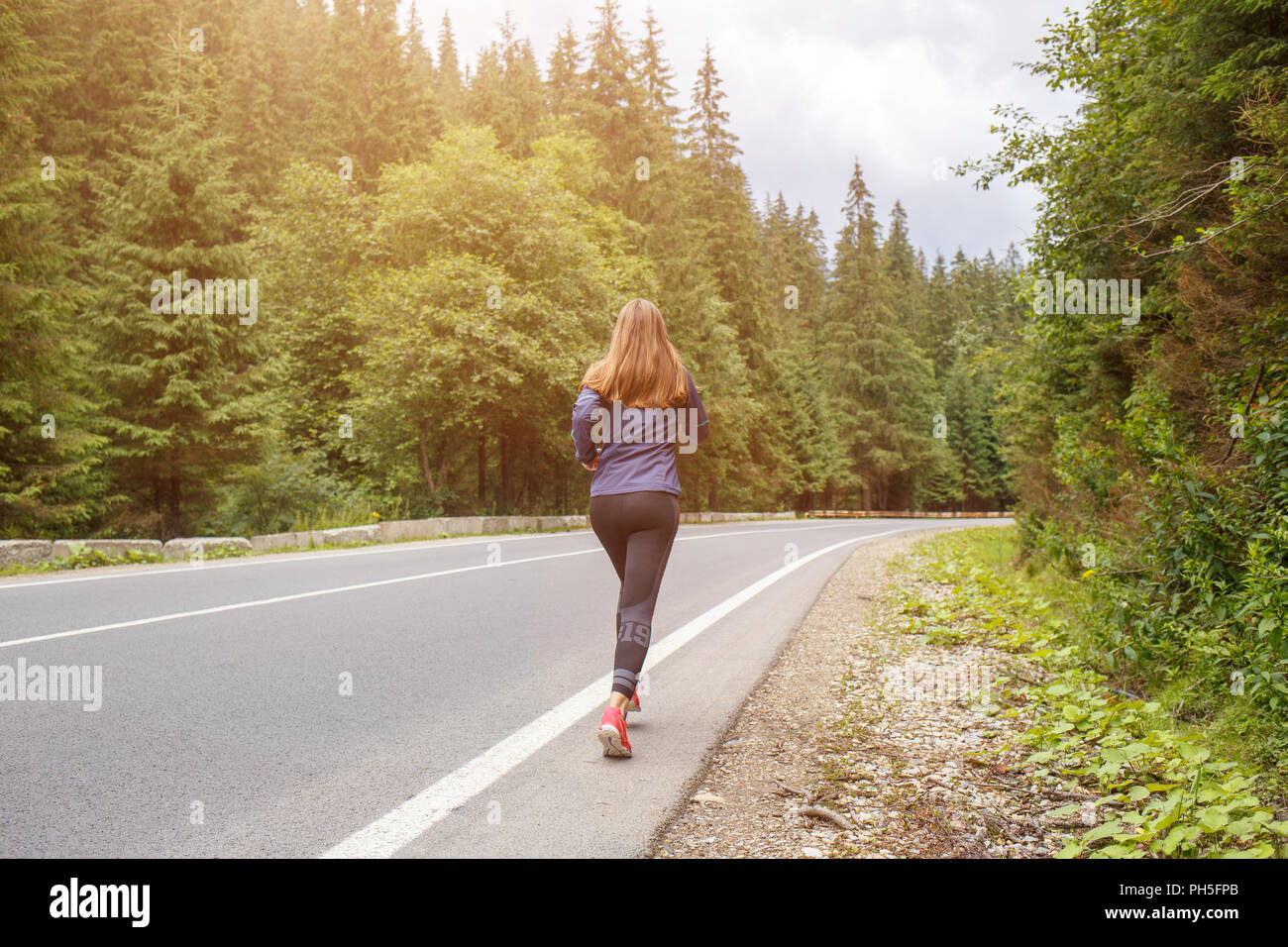 Running girl on the road. Young slim woman jogging in mountains. Rear ...