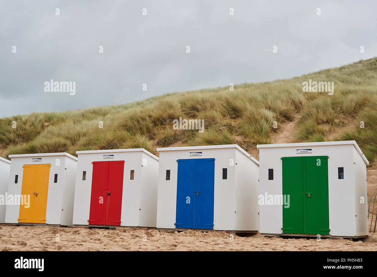 Four White Beach Huts with multicoloured doors, grass sand dunes and a ...