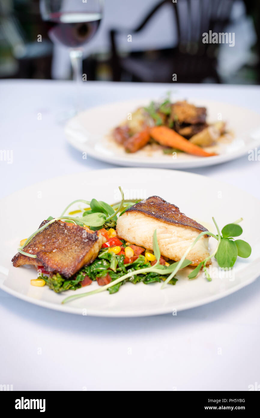 Pan roasted sable fish with spring vegetables on a white plate in a ...
