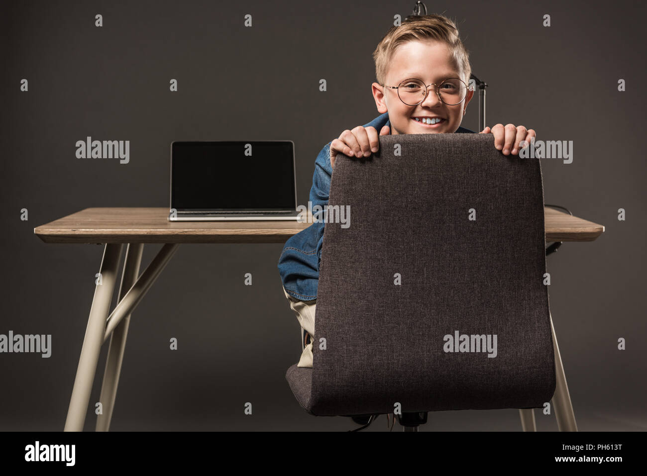 happy little boy sitting on chair and looking at camera near table with ...