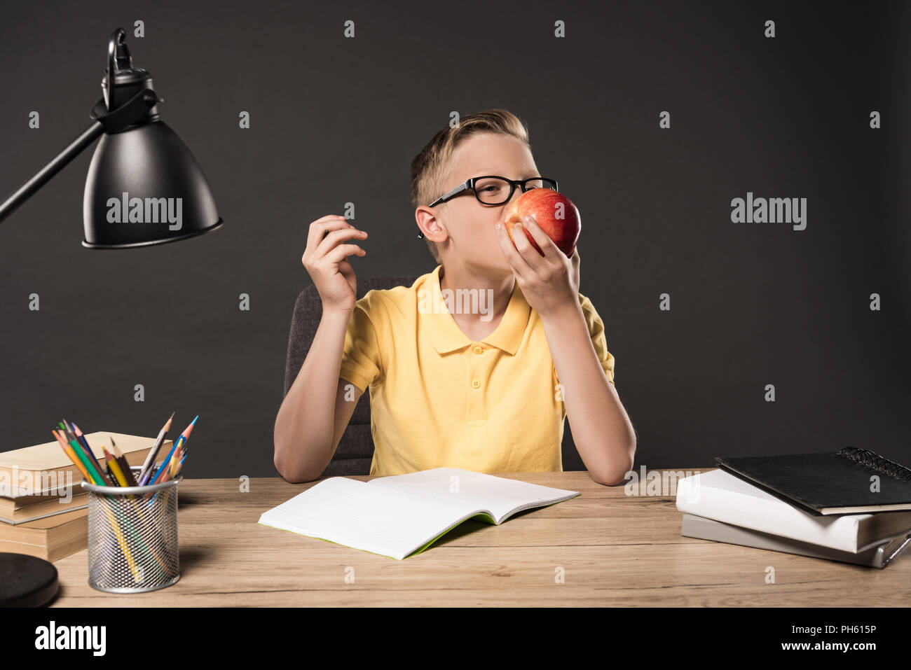 schoolboy in eyeglass eating apple and doing homework at table with ...
