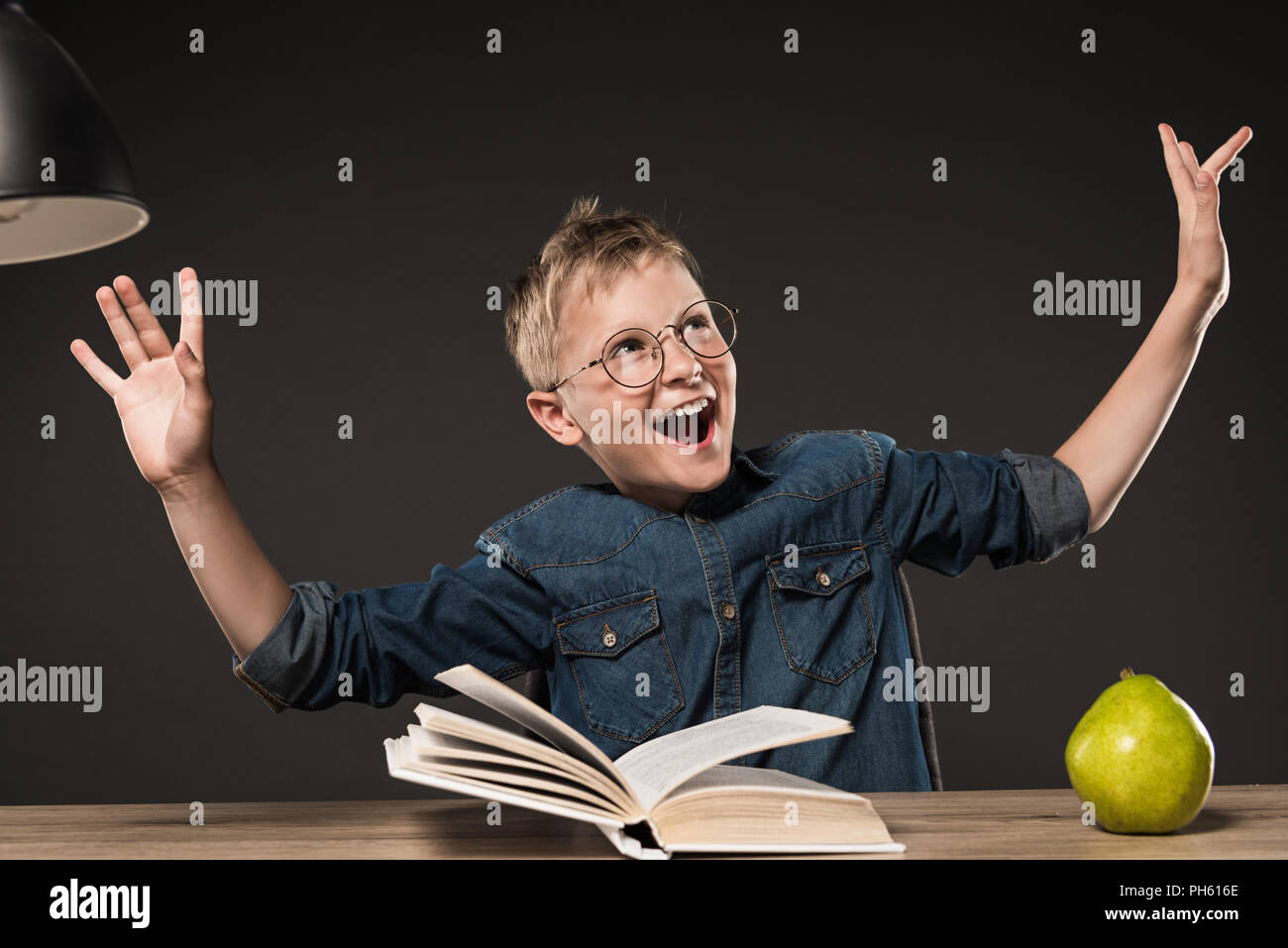 excited school boy in eyeglasses gesturing by hands while reading book ...