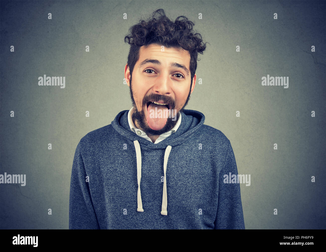 Young casual hipster man making faces and showing tongue at camera ...