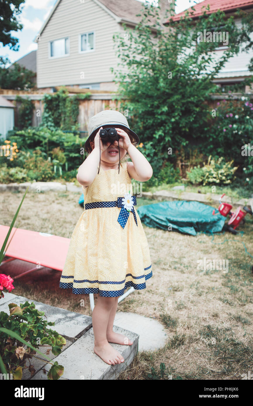 Portrait of cute Caucasian girl in yellow dress and hat looking through ...
