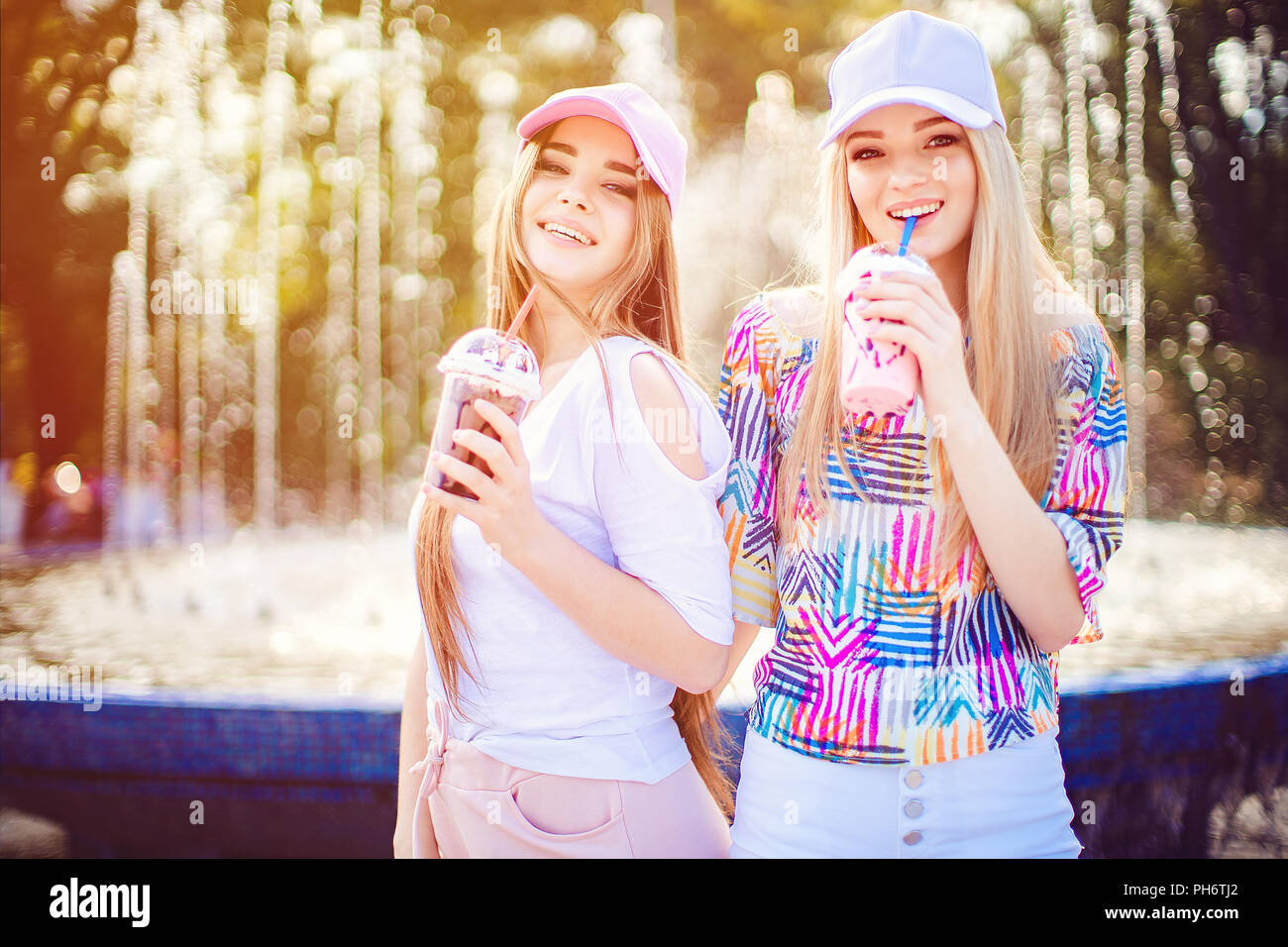 Two beautiful female friends with cold beverages laughing and having ...