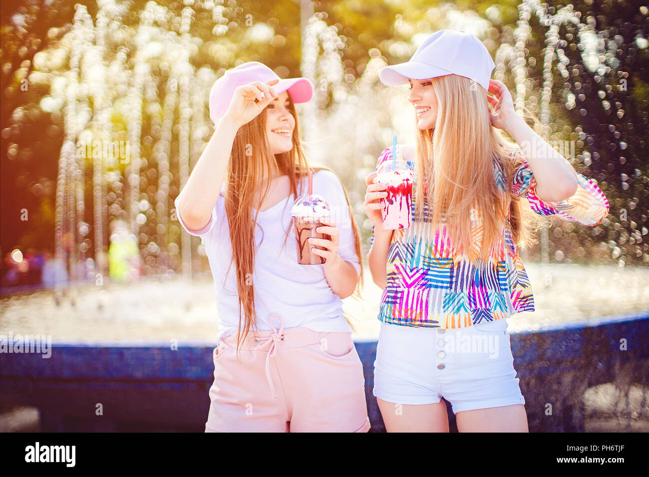 Two beautiful female friends with cold beverages laughing and having ...