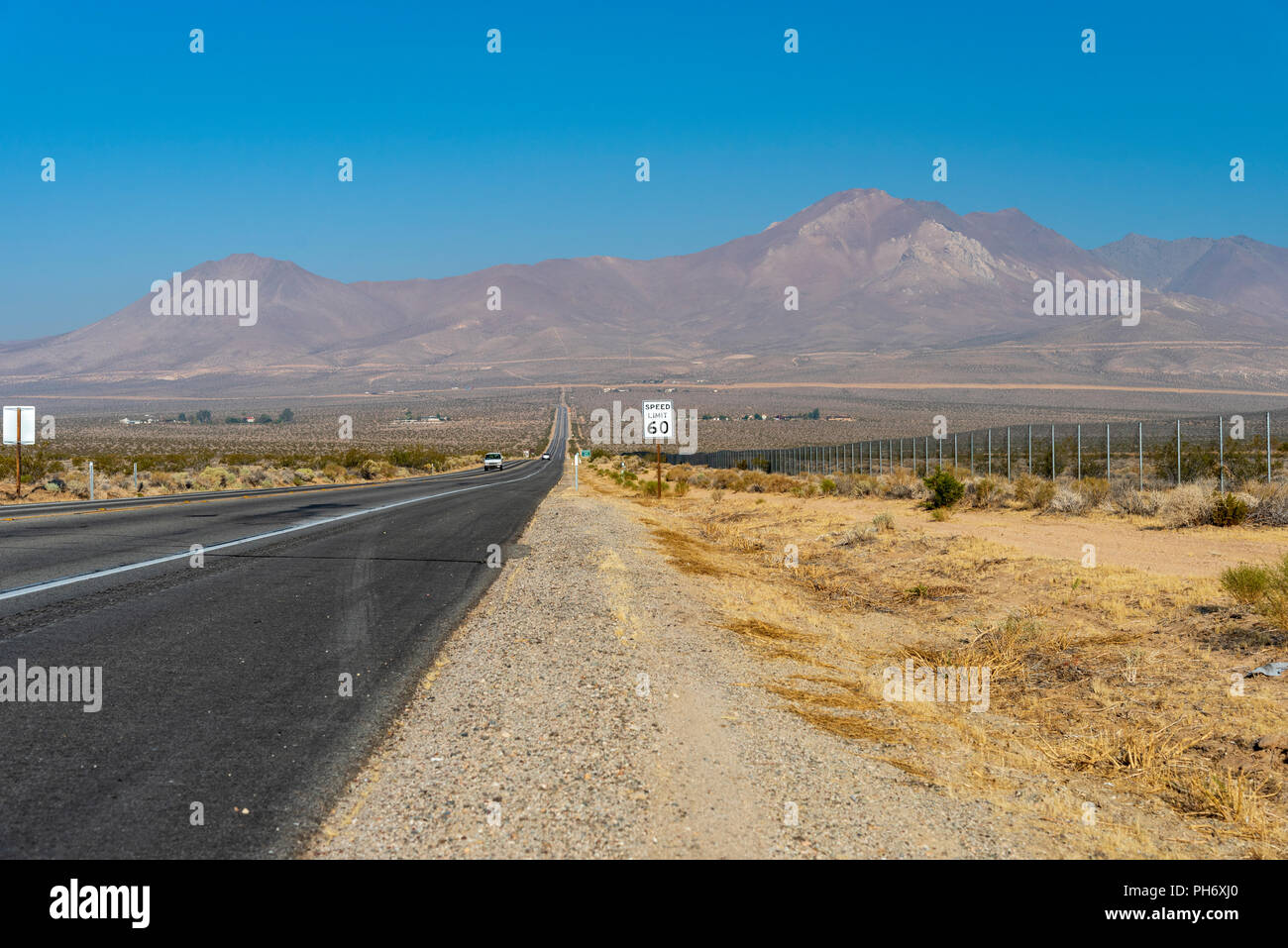 Desert highway with speed limit sign leading towards tall barren ...