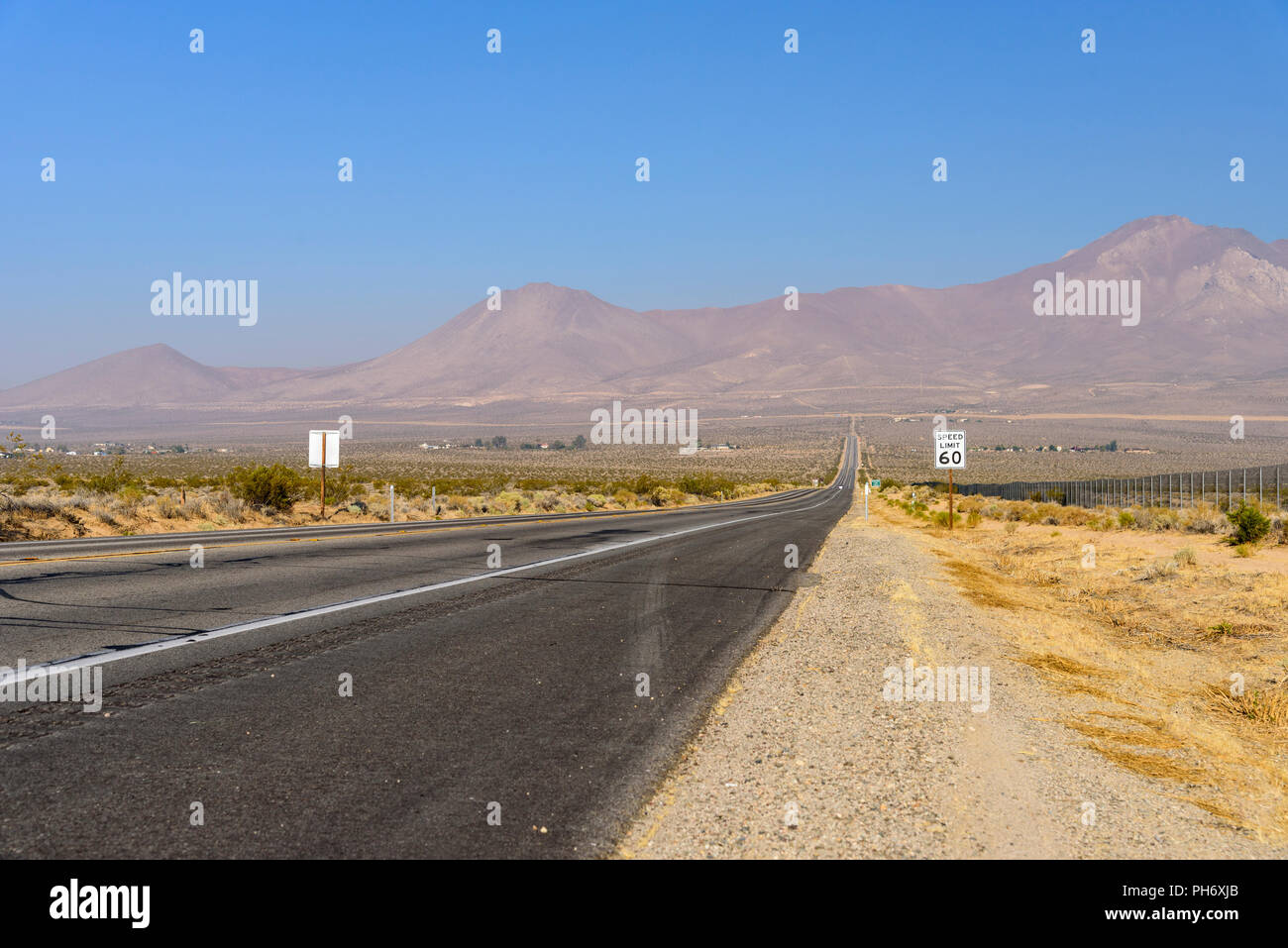 Desert highway with speed limit sign leading towards tall barren ...