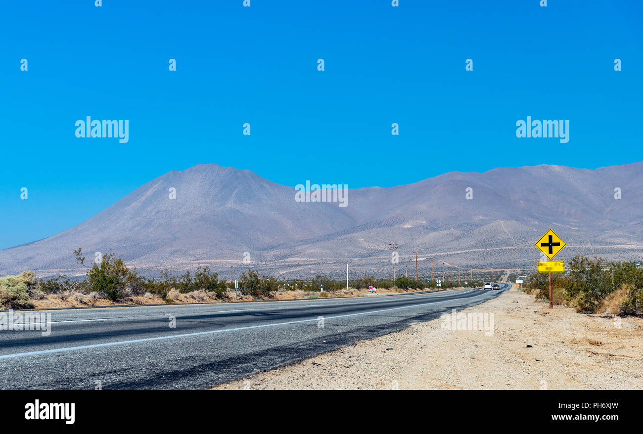 Desert road leading towards mountains under a bright blue sky with ...