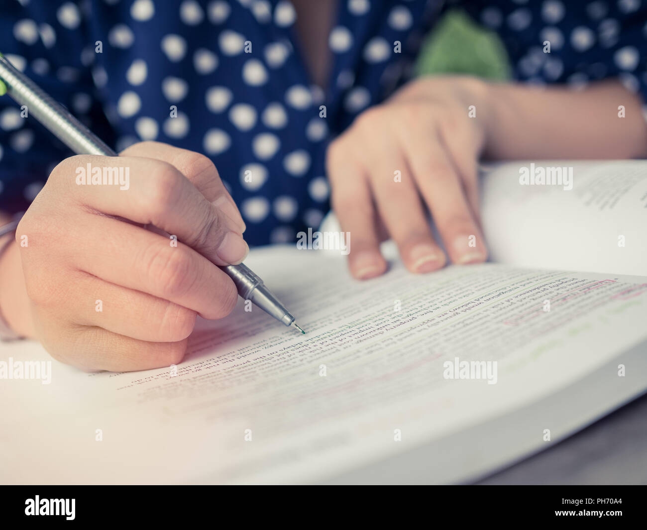 Close-up hand holding a pen and reading book. Woman wearing polka dot ...