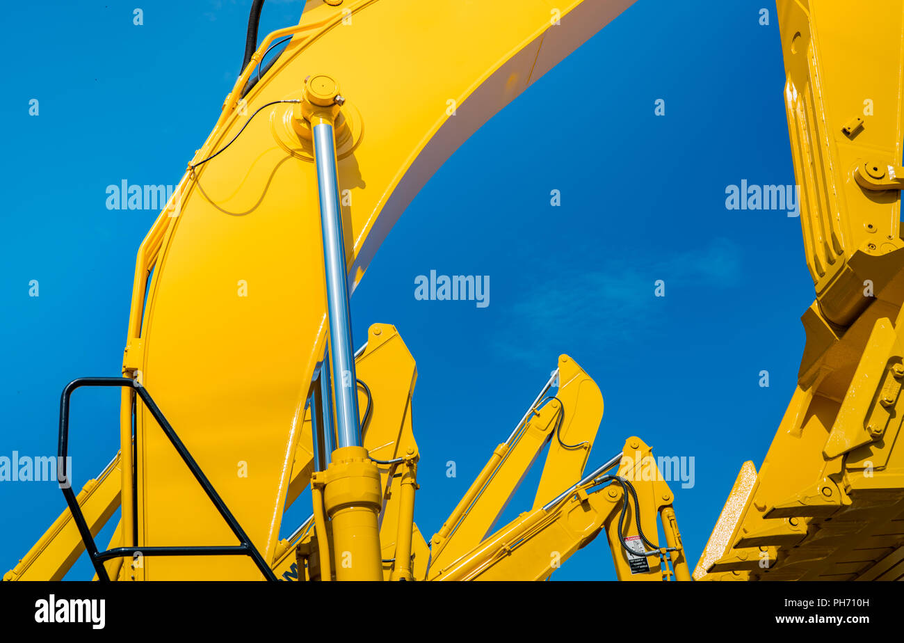 Yellow backhoe with hydraulic piston arm against clear blue sky. Heavy ...