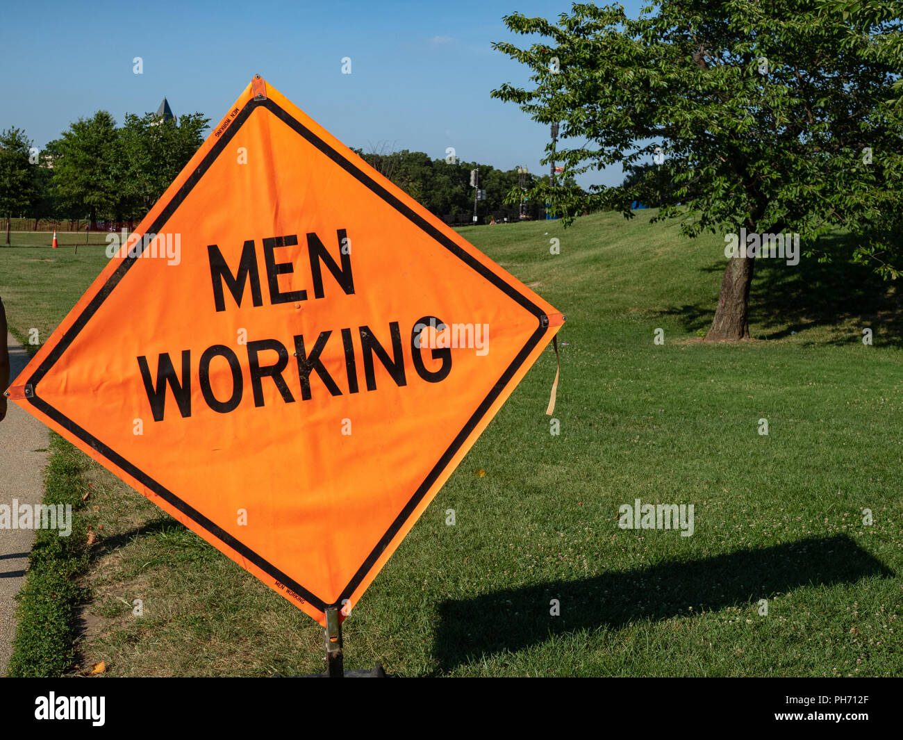 A men working constrction sign posted up in a park area Stock Photo - Alamy