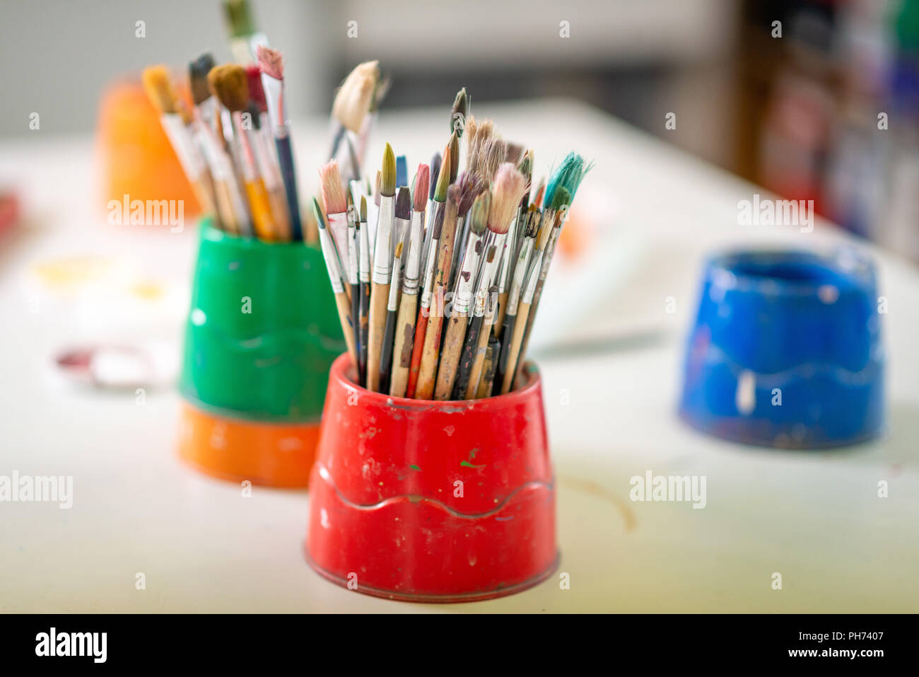 Pots of artist's used paint brushes on a school desk photographed in ...